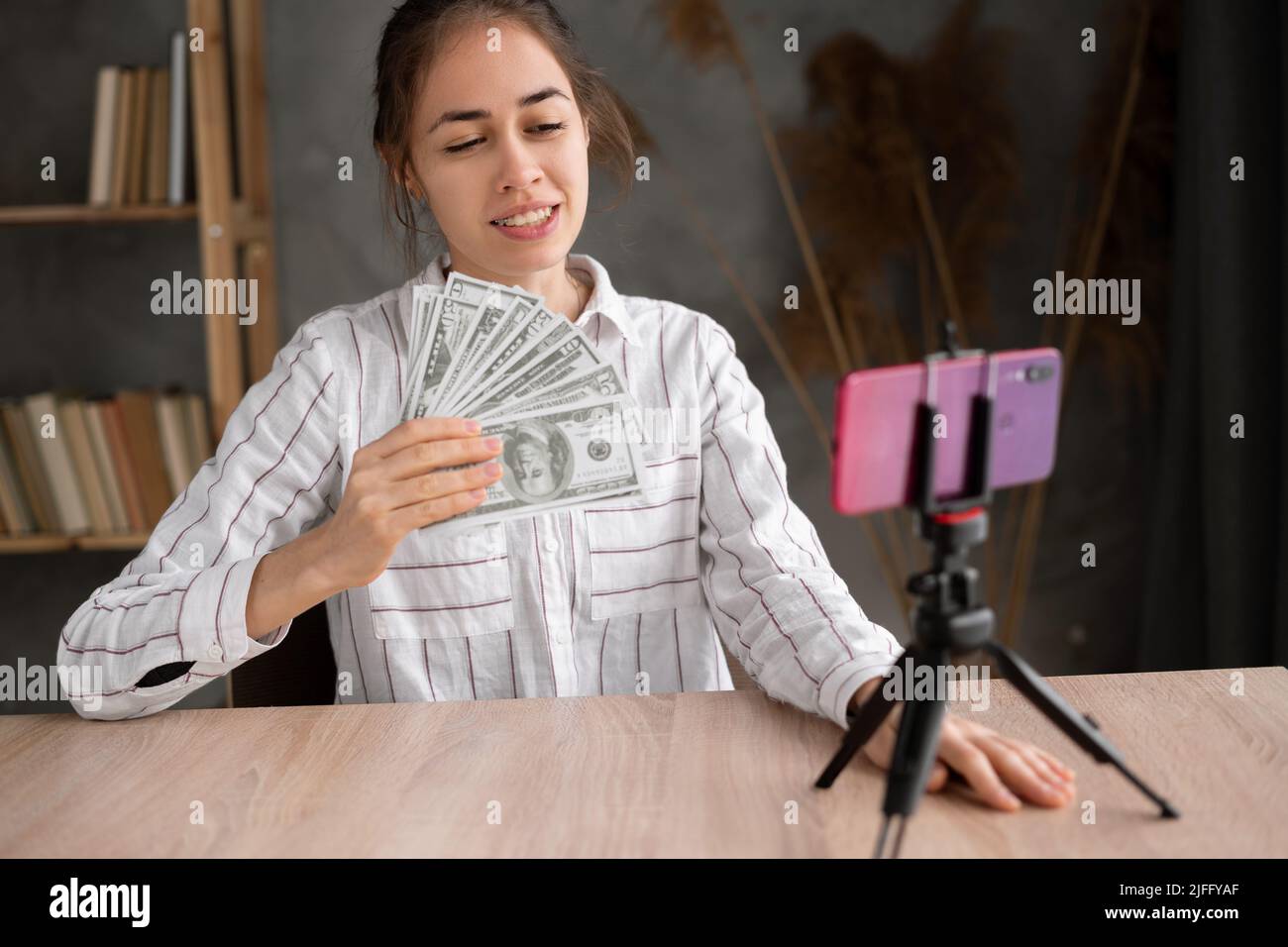 Young hispanic woman showing bunch of dollar banknotes on her mobile ...