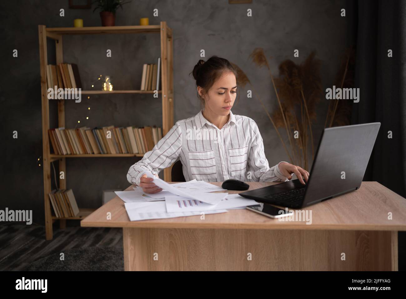 Focused businesswoman working on laptop holding papers preparing report ...