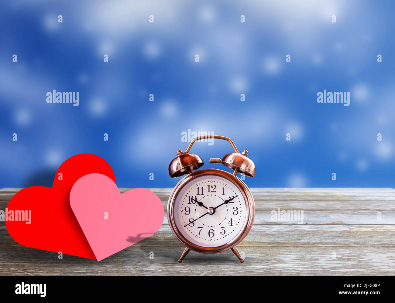 Red and pink heart and vintage alarm clock on wood panel table with ...