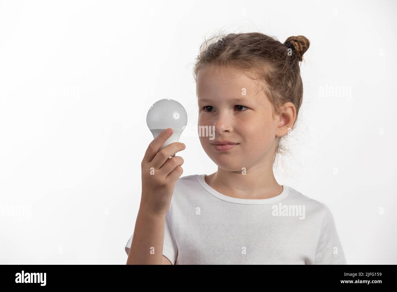 Child holding a LED light bulb in her hand with a white background. A ...