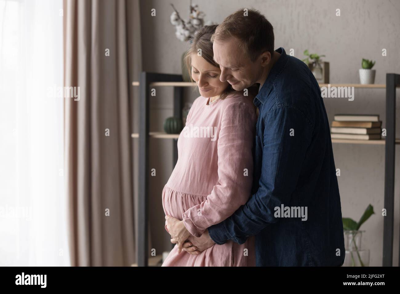 Loving future parents expecting their first baby hugging standing ...