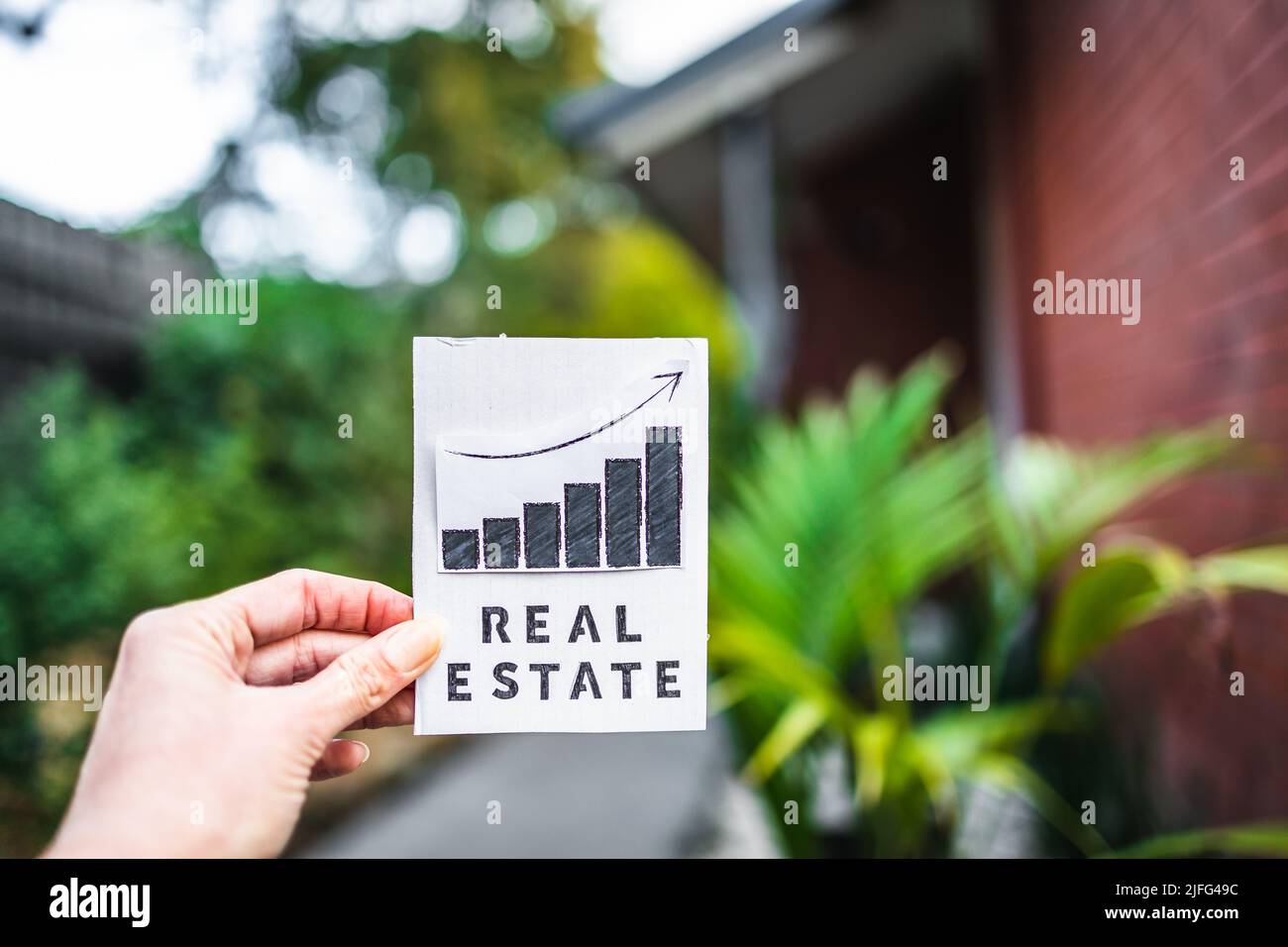 hand holding real estate sign with graph showing stats going up in ...