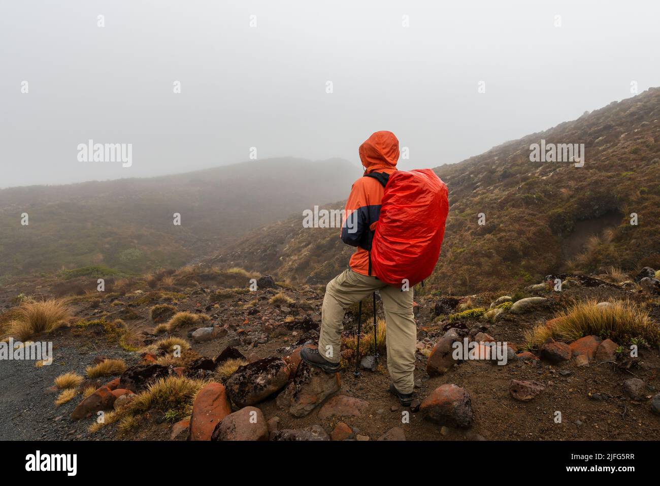 Hiking Tama Lakes track in thick fog and rain, among red coloured rocks ...