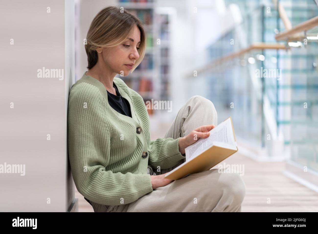 Focused pensive middle-aged woman passionate reader reading book while ...