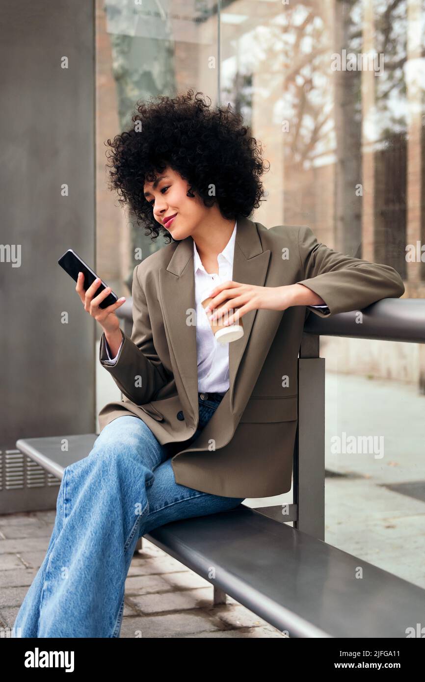 young woman using her phone while waiting the bus Stock Photo - Alamy