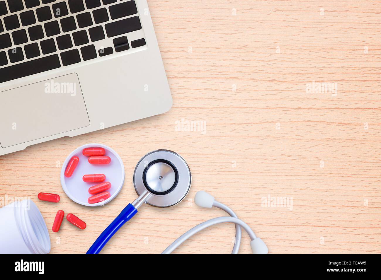 Laptop computer and pill with blue stethoscope on wooden desk. Top view ...