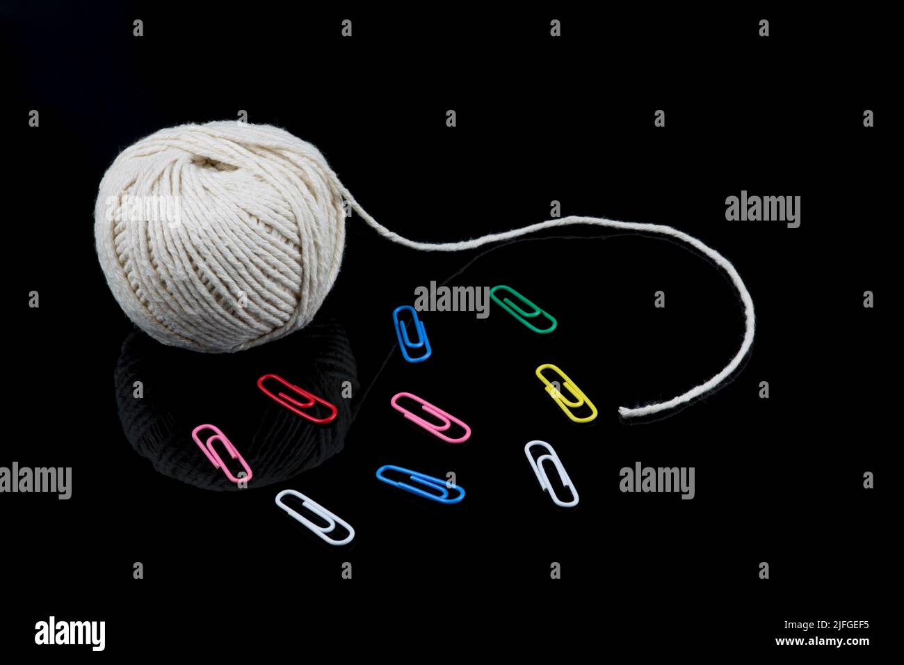 Ball of string and coloured paper clips isolated on a shiny black ...