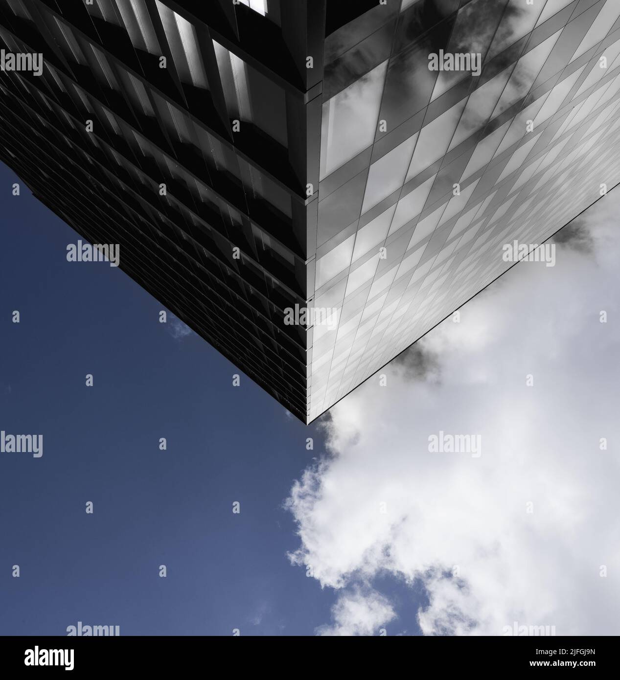 A vertical upside down of a modern skyscraper against a cloudy blue sky ...