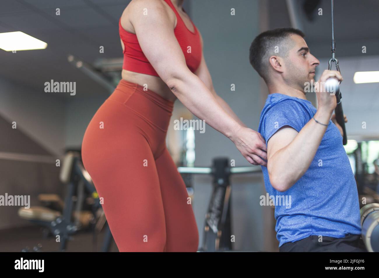 Young personal trainer helps to client on gym station adjusting back ...