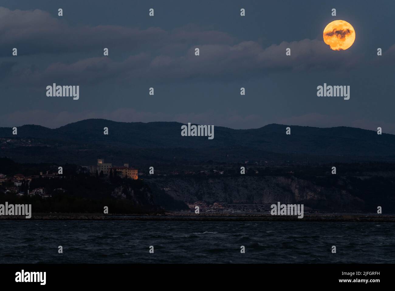 A view of the full moon rising above the sea, with castle and coast ...
