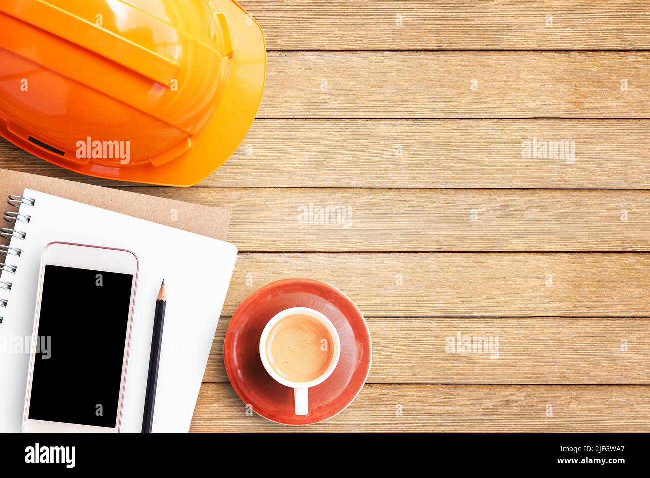 Safety helmet, blank paper notebook and smart phone on brown wooden ...