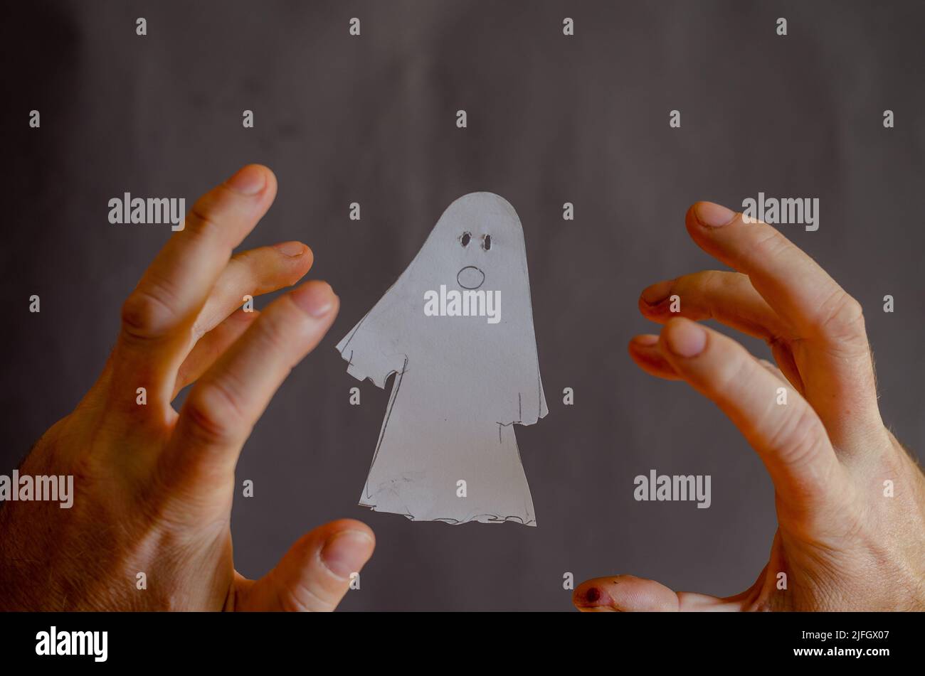 Hands of a man with bent fingers around a white paper ghost. Halloween ...