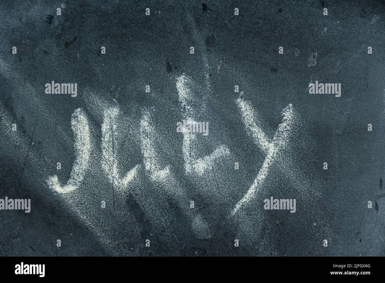 Semi-erased word JULY on black chalkboard. Handwritten word. Fuzzy ...