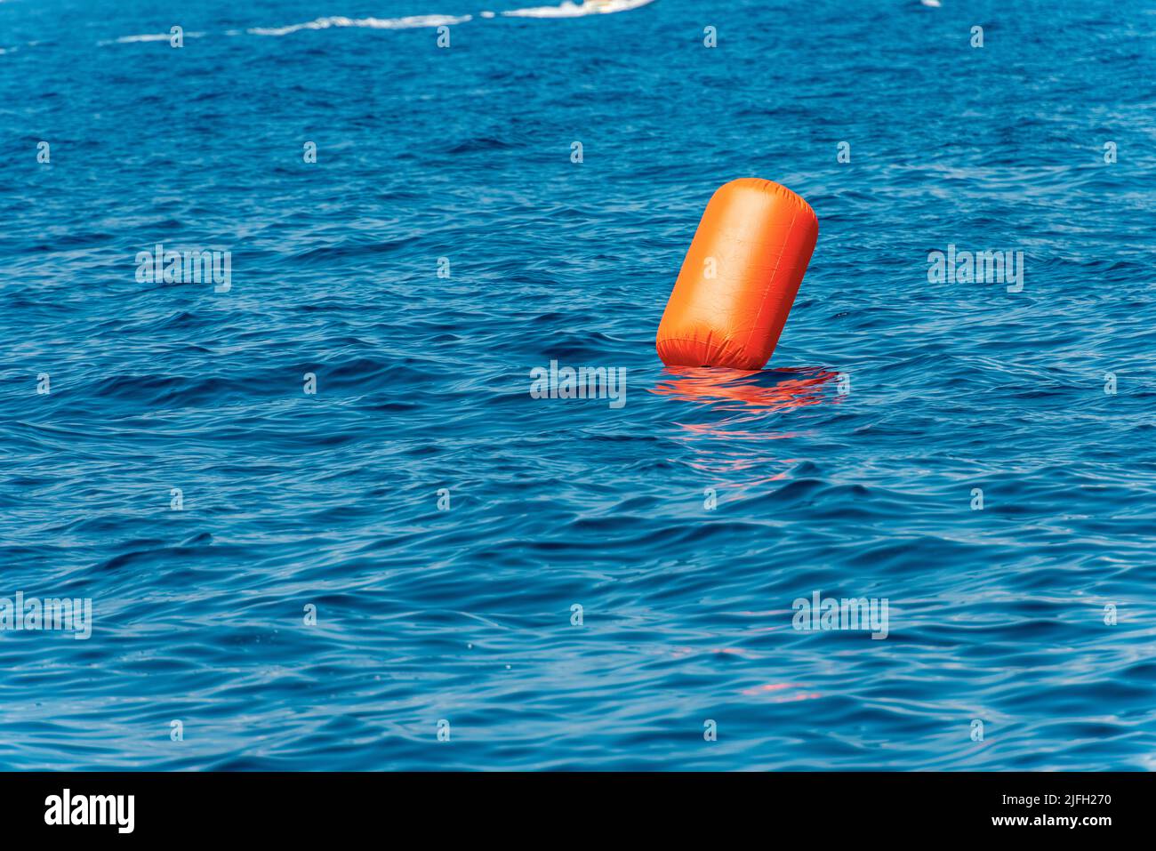 One large orange inflatable signal buoy floating in the blue ...