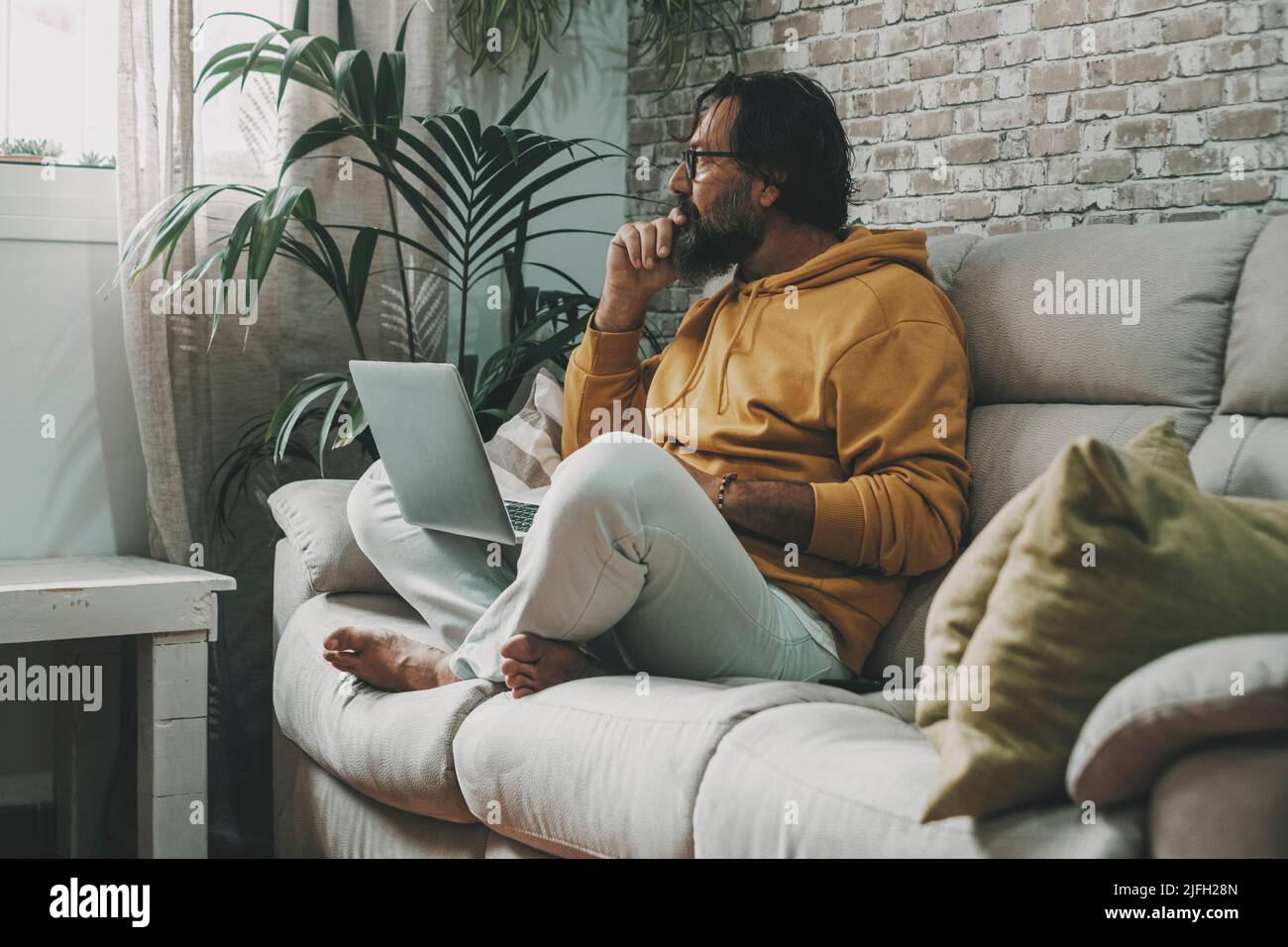 Mature man sitting at home with crossed legs and working on laptop ...