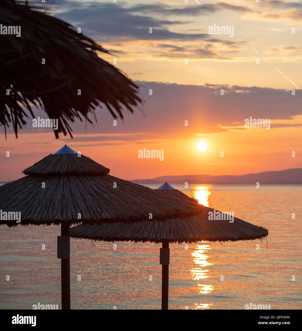 Sunset on the beach over Aegean Sea, Greece. Straw umbrellas silhouette ...