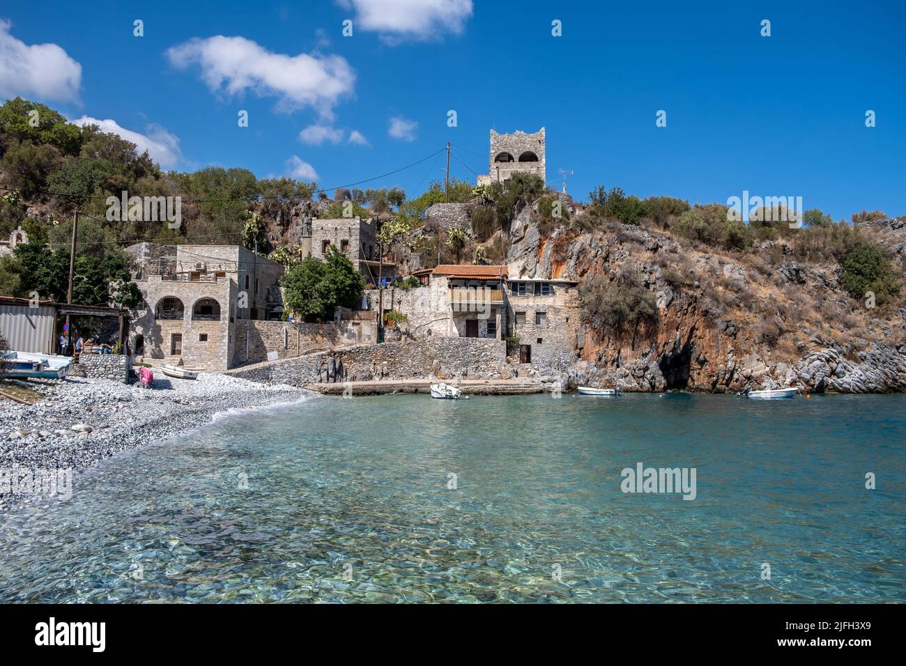 Greece. Alypa pebble beach, moored boat in transparent calm sea, ruin ...