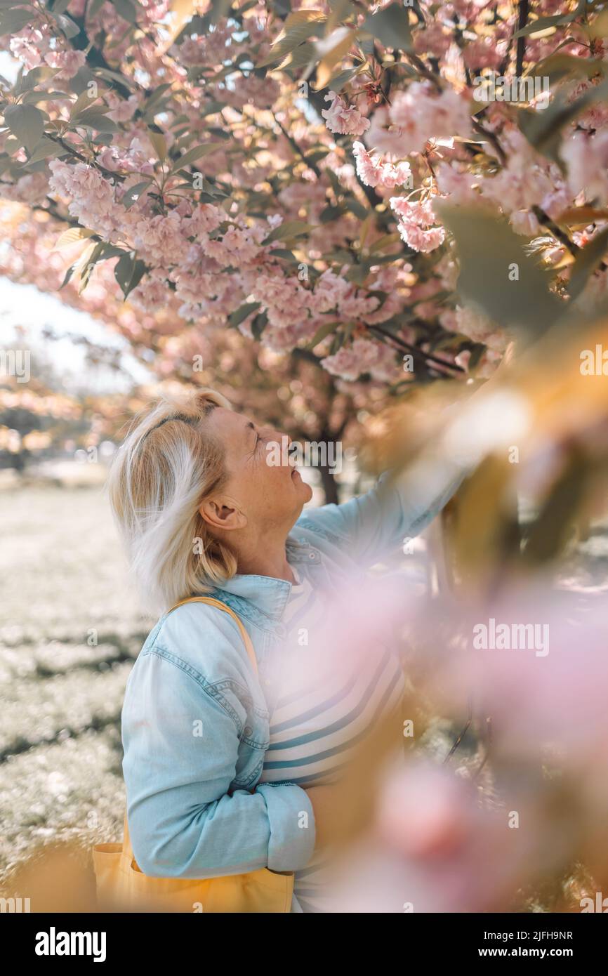Beautiful 50s woman enjoying sunny day in park during cherry blossom ...