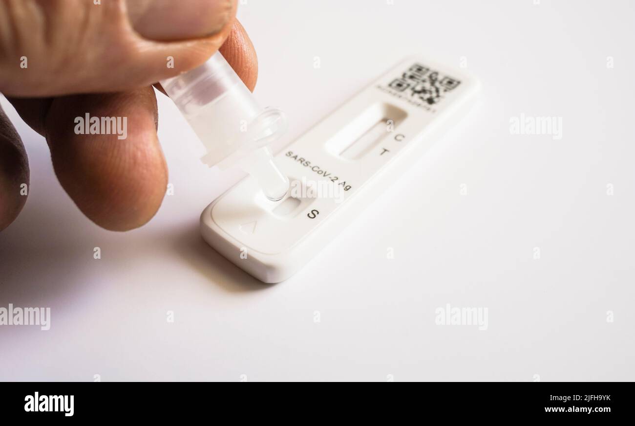 A covid swab sample in solution is dropped onto the test cassette of a ...
