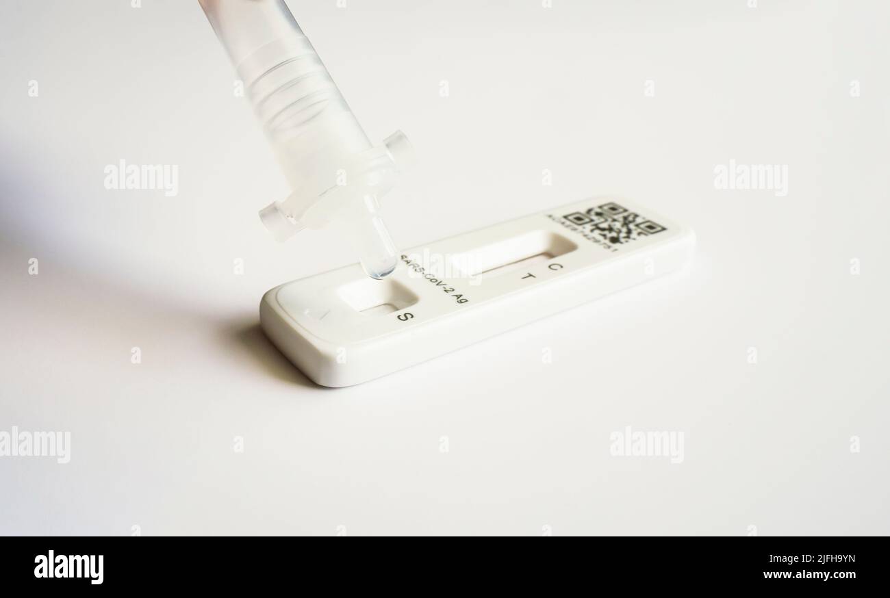 A covid swab sample in solution is dropped onto the test cassette of a ...