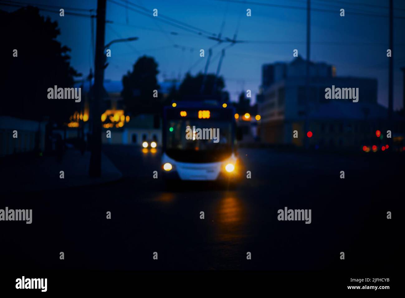 A blurry image of a trolleybus with its headlights on, driving through ...