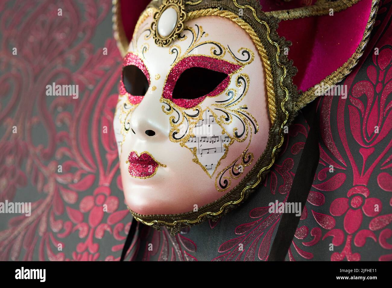 A red and gold Venetian mask hangs on decorative wallpaper Stock Photo ...