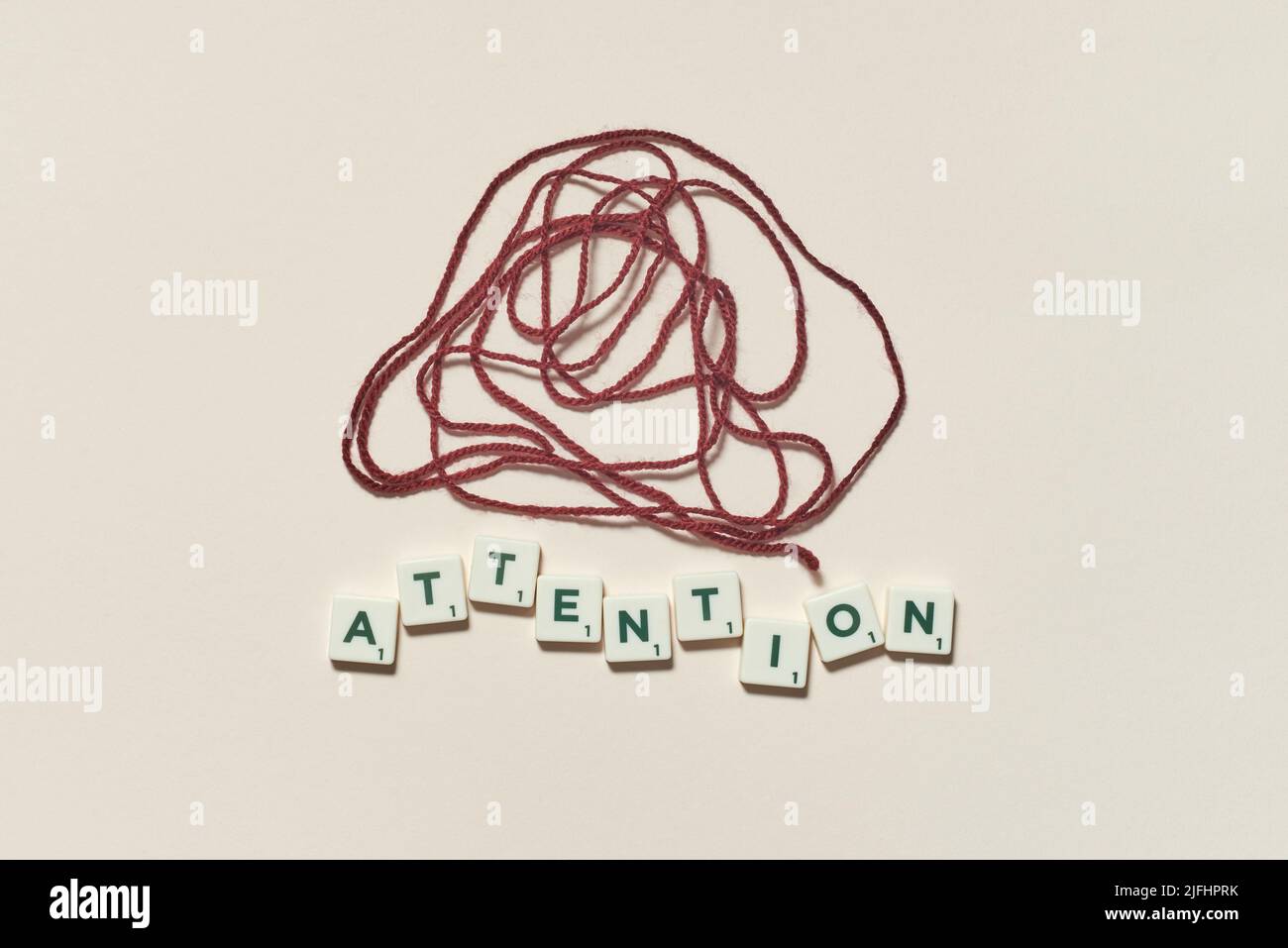 Attention word formed of scrabble tiles with tangled thread over beige ...