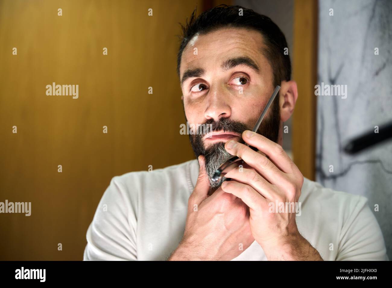 Young man with a beard shaving with a traditional knife in front of the ...