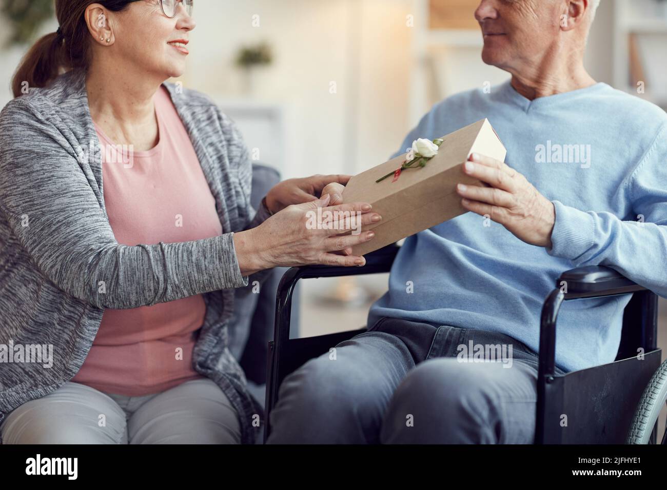 Close-up of smiling wife in glasses giving gift box with attached ...