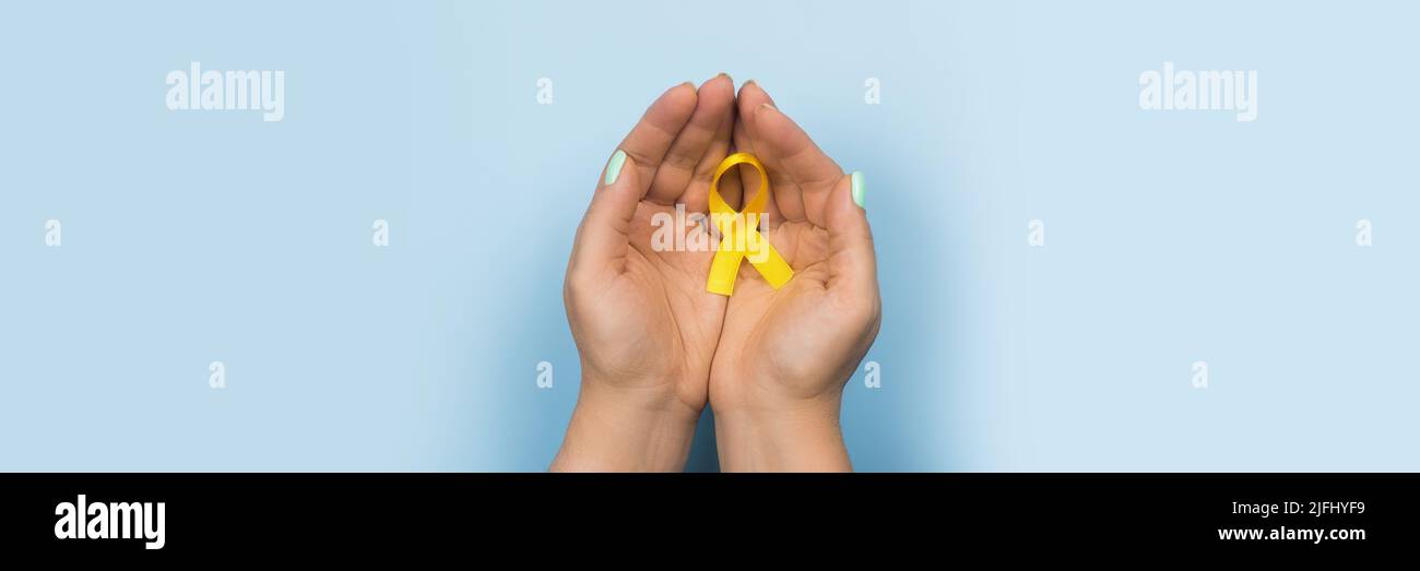 Yellow gold ribbon in the hands of a girl on a blue background ...