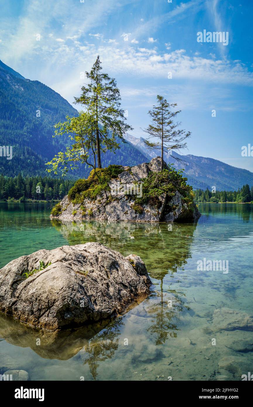 A vertical shot of trees on a rock at the middle of a scenic alpine ...