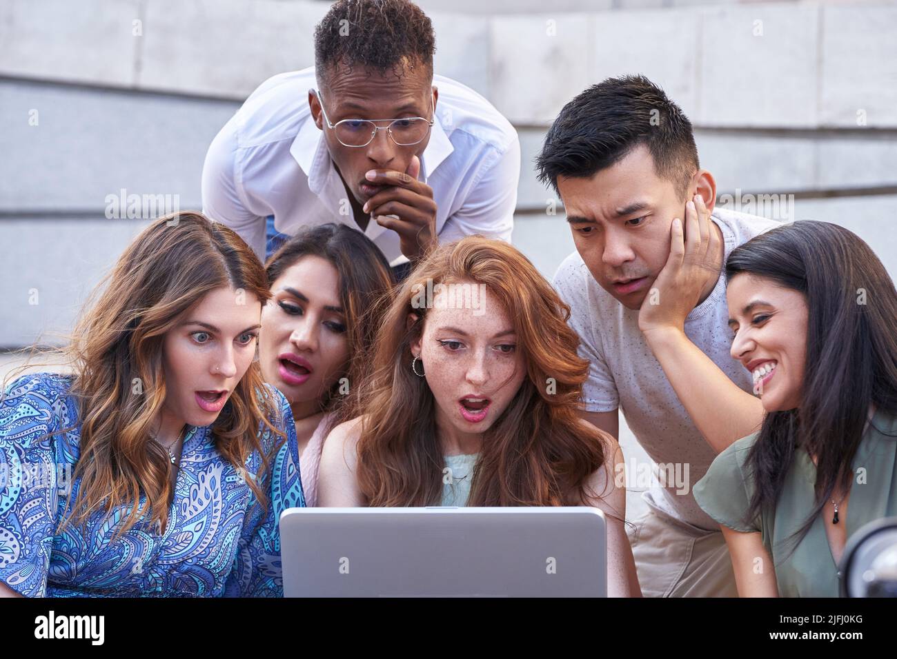 Group of multi-ethnic people look at laptop screen with a shocked ...