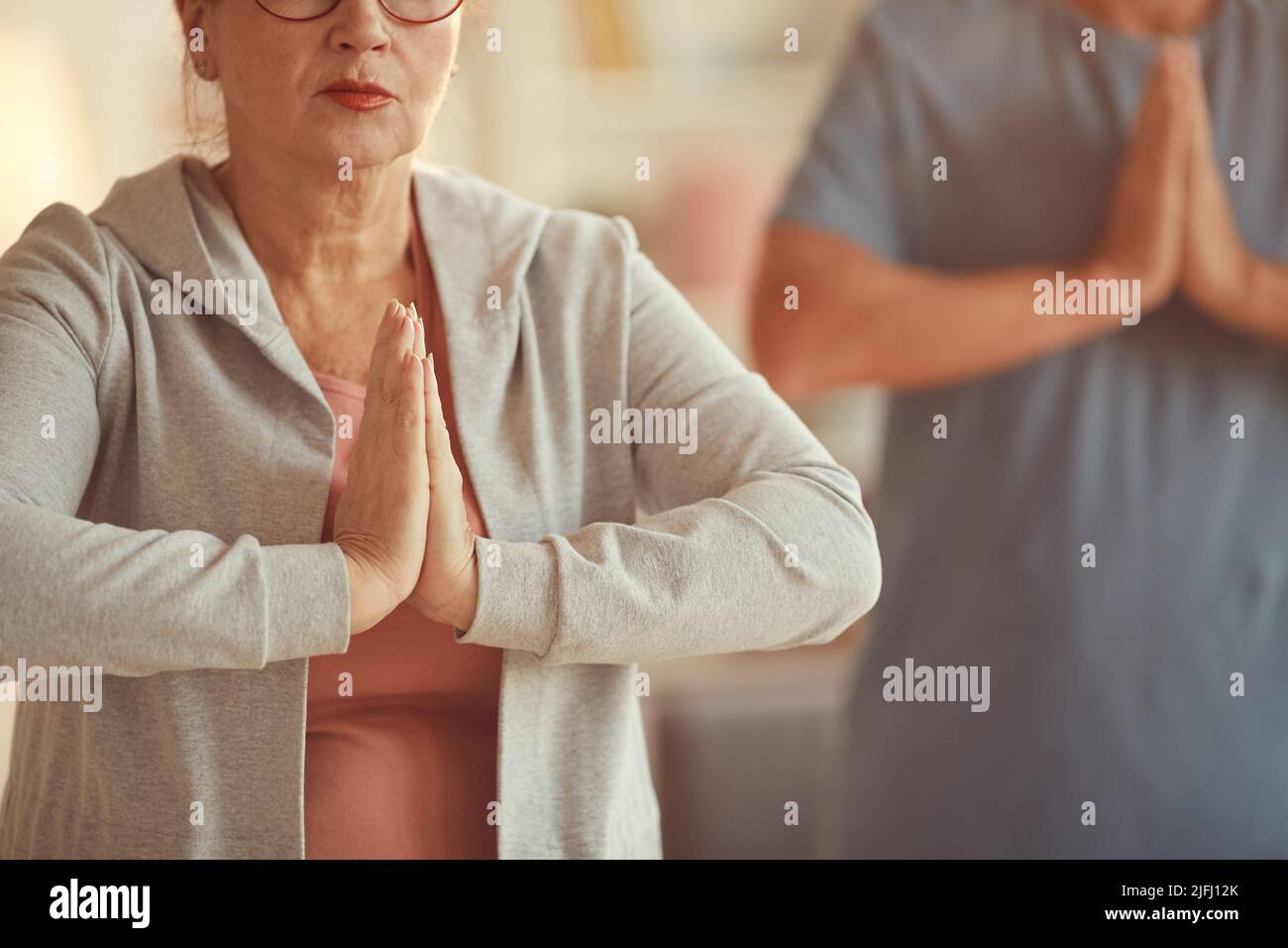 Close-up of calm senior woman in sports shirt holding hands in mudra ...