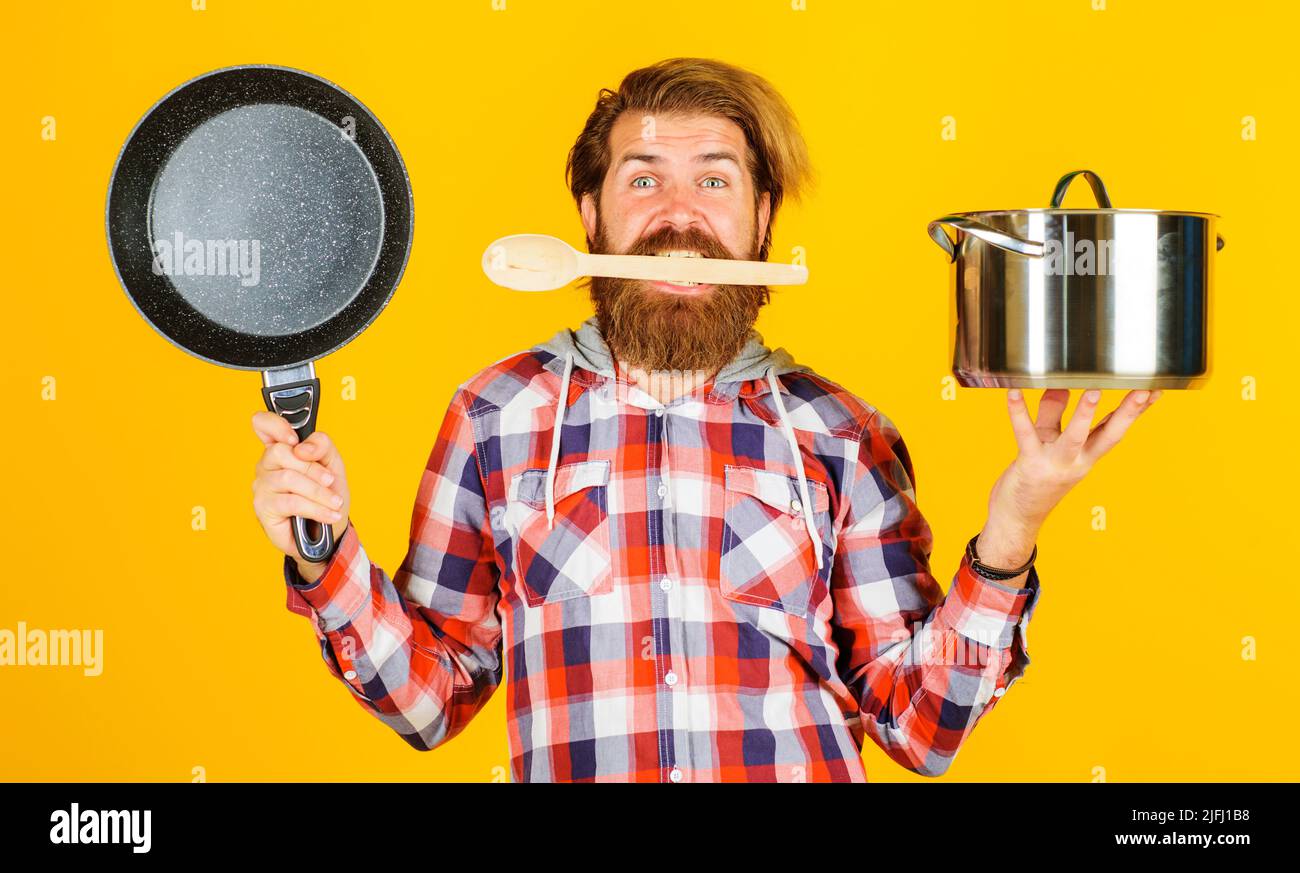 Man with saucepan and frying pan in hands. Bearded chef with wooden ...