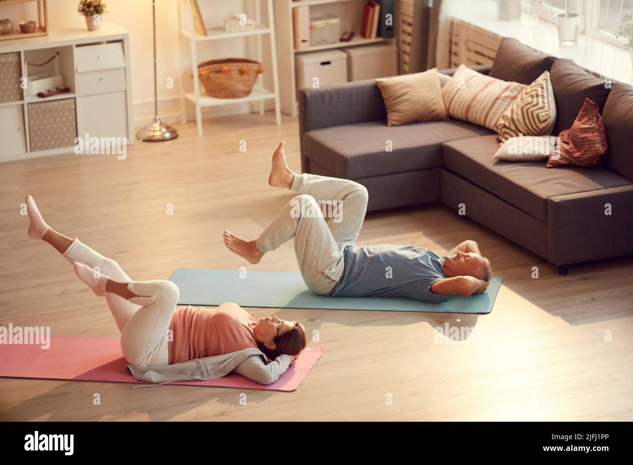 Healthy senior couple lying on mats in living room and rotating legs ...