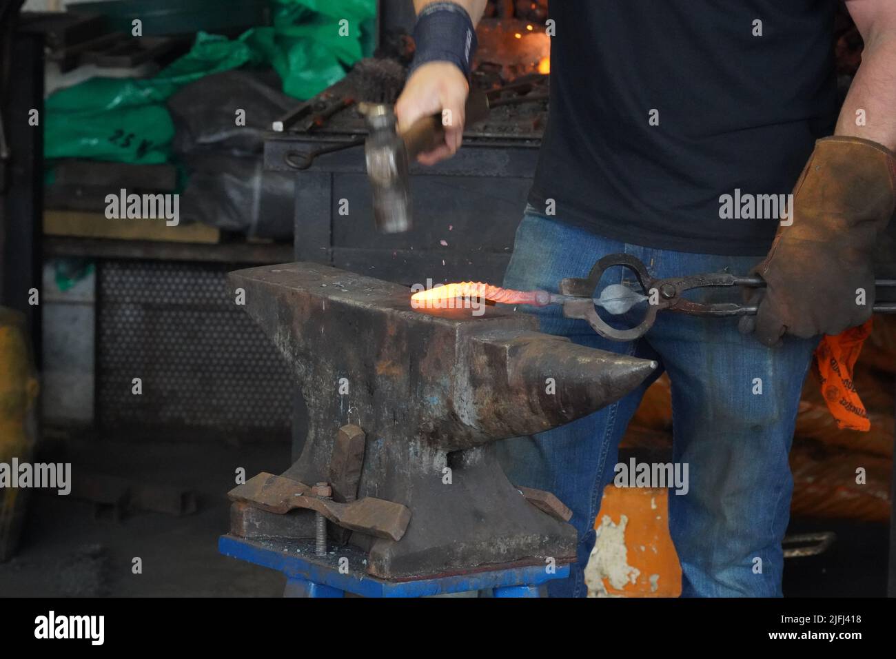 Close-up of the hands of a blacksmith using a hammer and anvil to shape ...