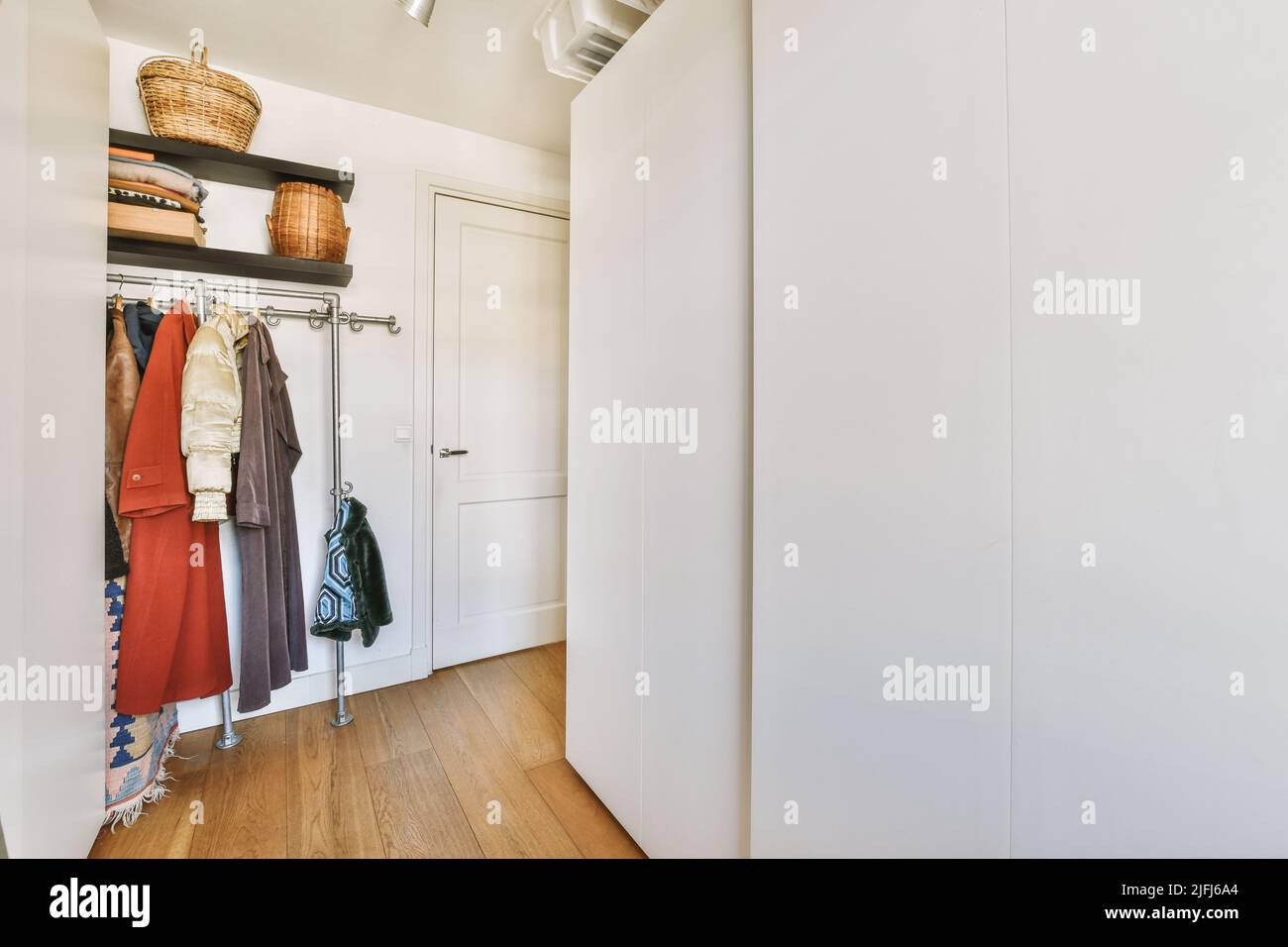 Light narrow dressing room with a wooden floor, white cabinets, shelves ...