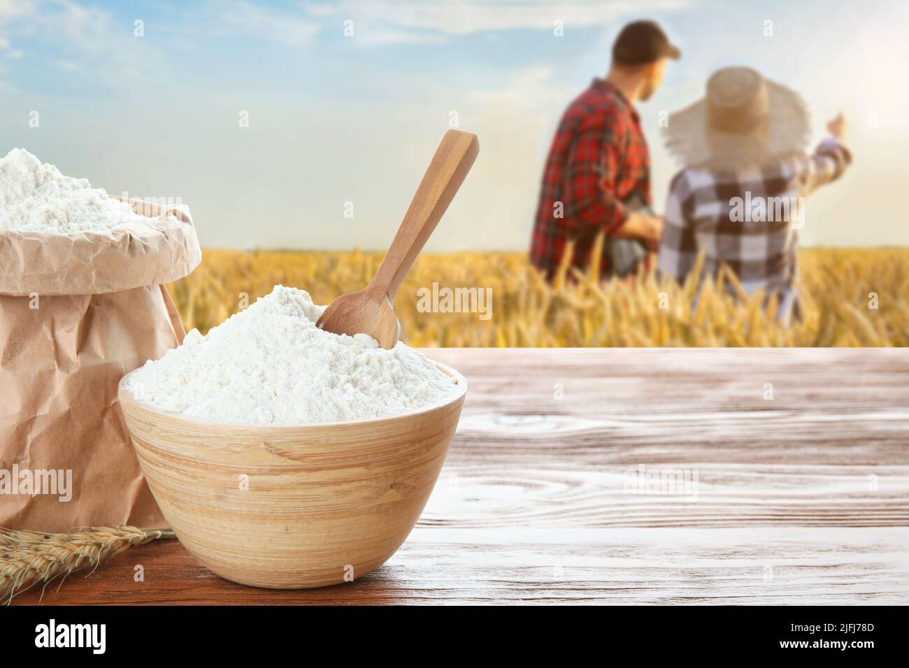 Bowl and paper bag with wheat flour on table in field with farmers ...