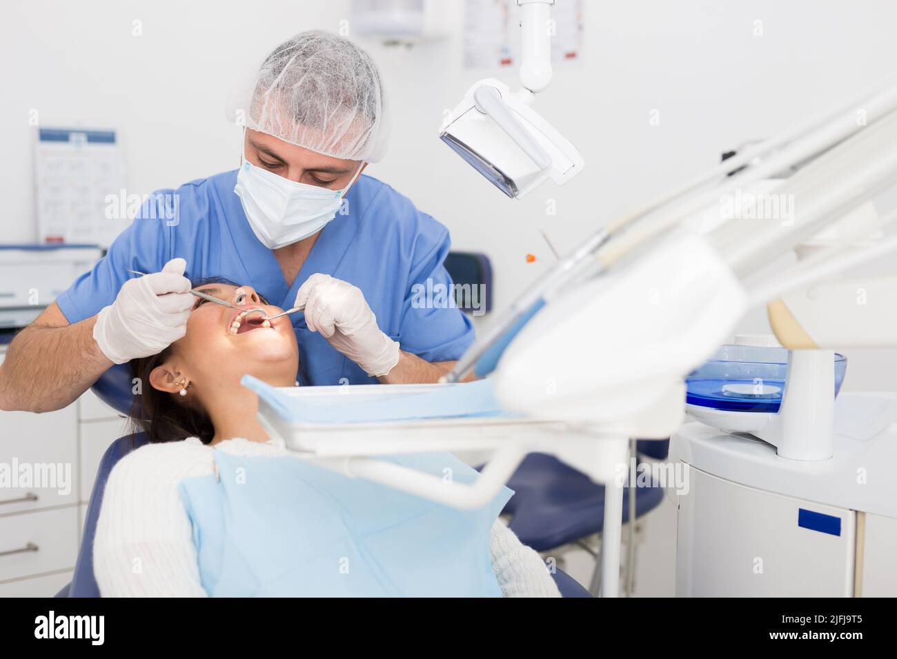 Dentist man examining a latin female patient teeth Stock Photo - Alamy