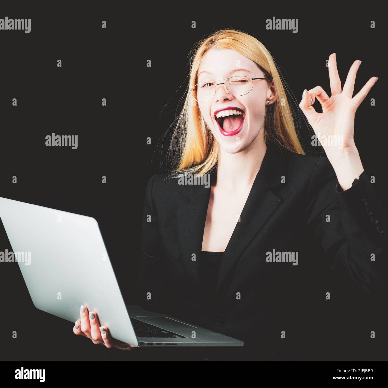 Portrait young shocked business woman winking in front of laptop computer looking at camera ...