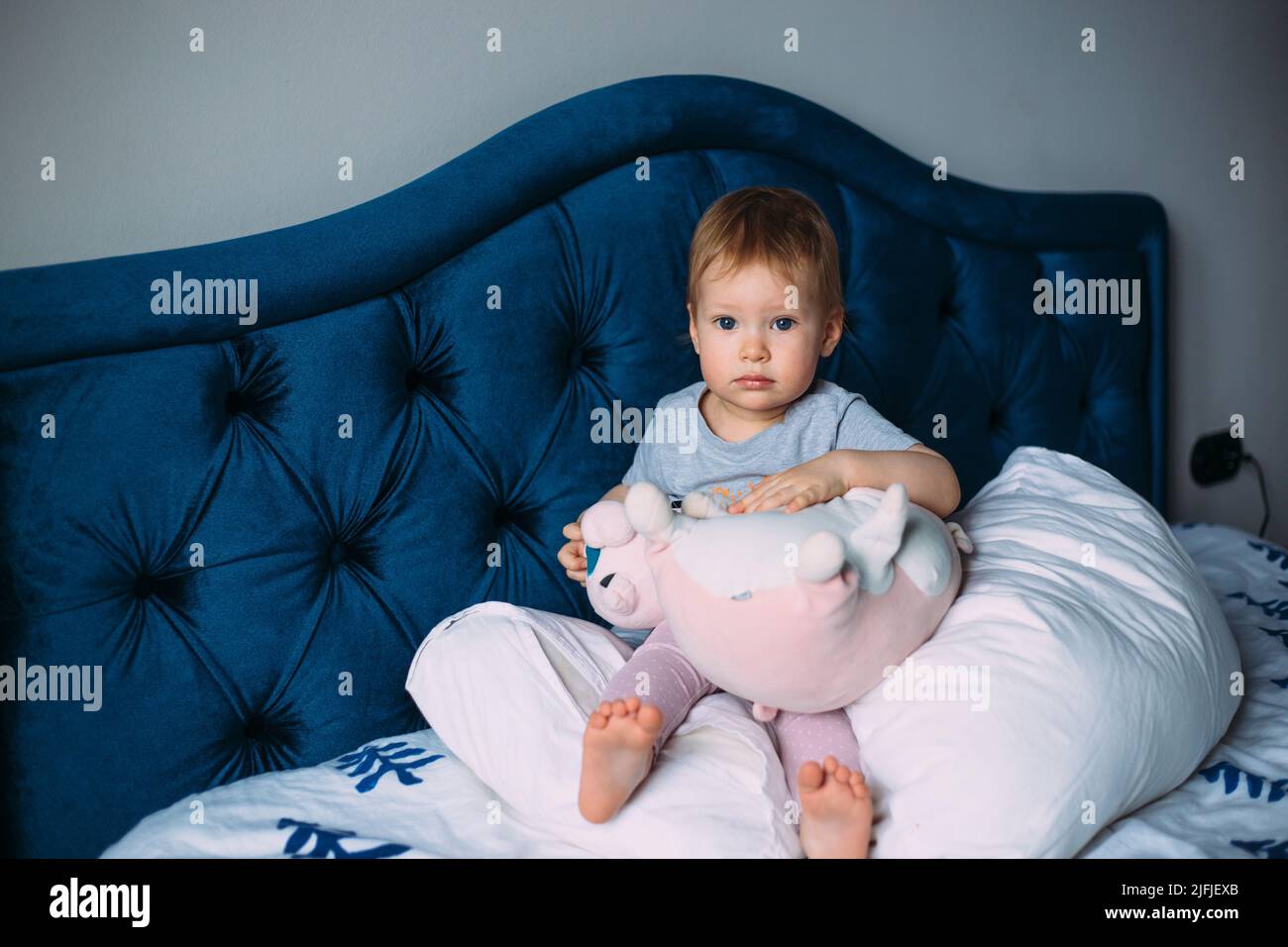 Funny little child is having fun, playing with soft toys on the couch ...