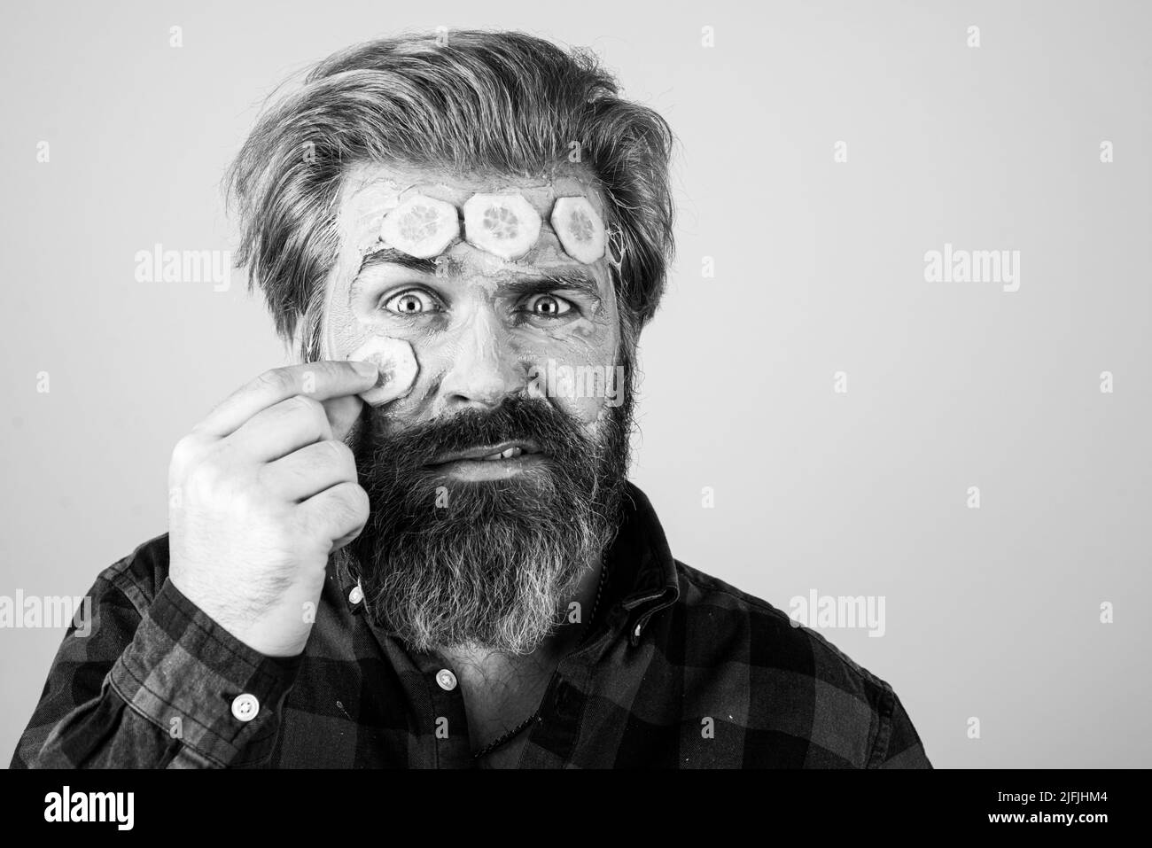 Funny male model with clay mask and cucumber slices on face. Spa ...