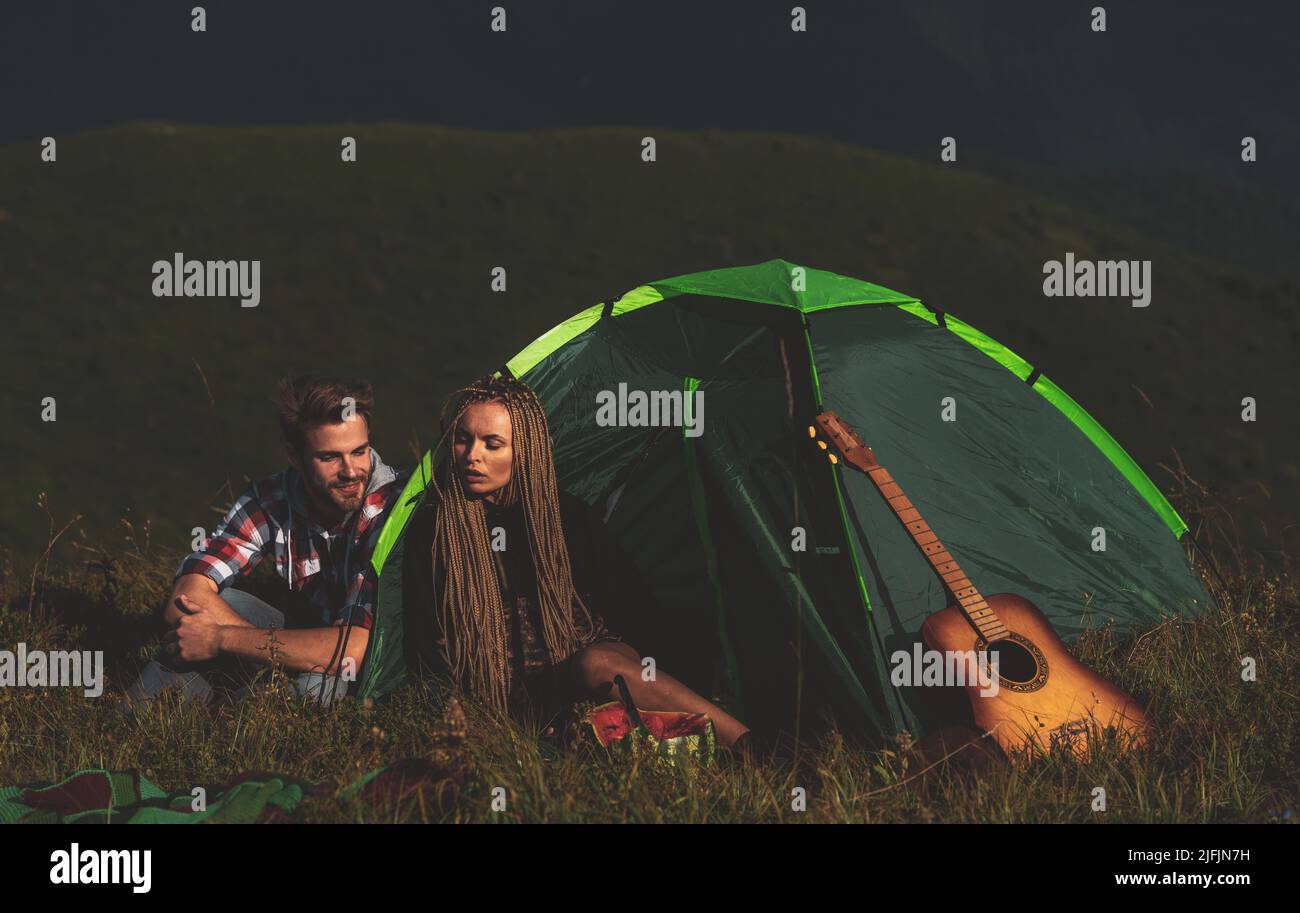 Camping. Happy man and woman smiling and playing songs at the guitar ...
