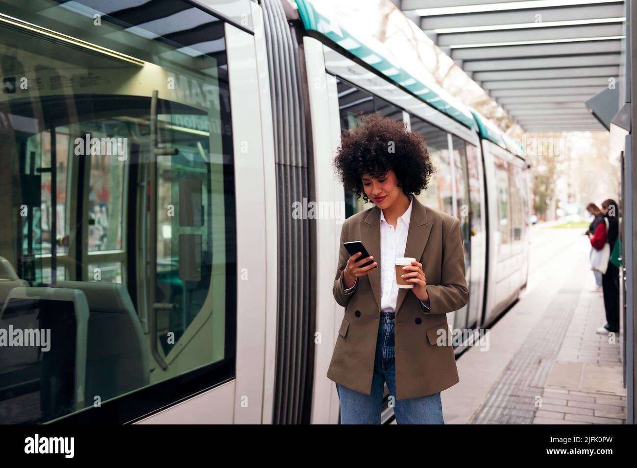 woman checking phone while waiting for the tram Stock Photo - Alamy