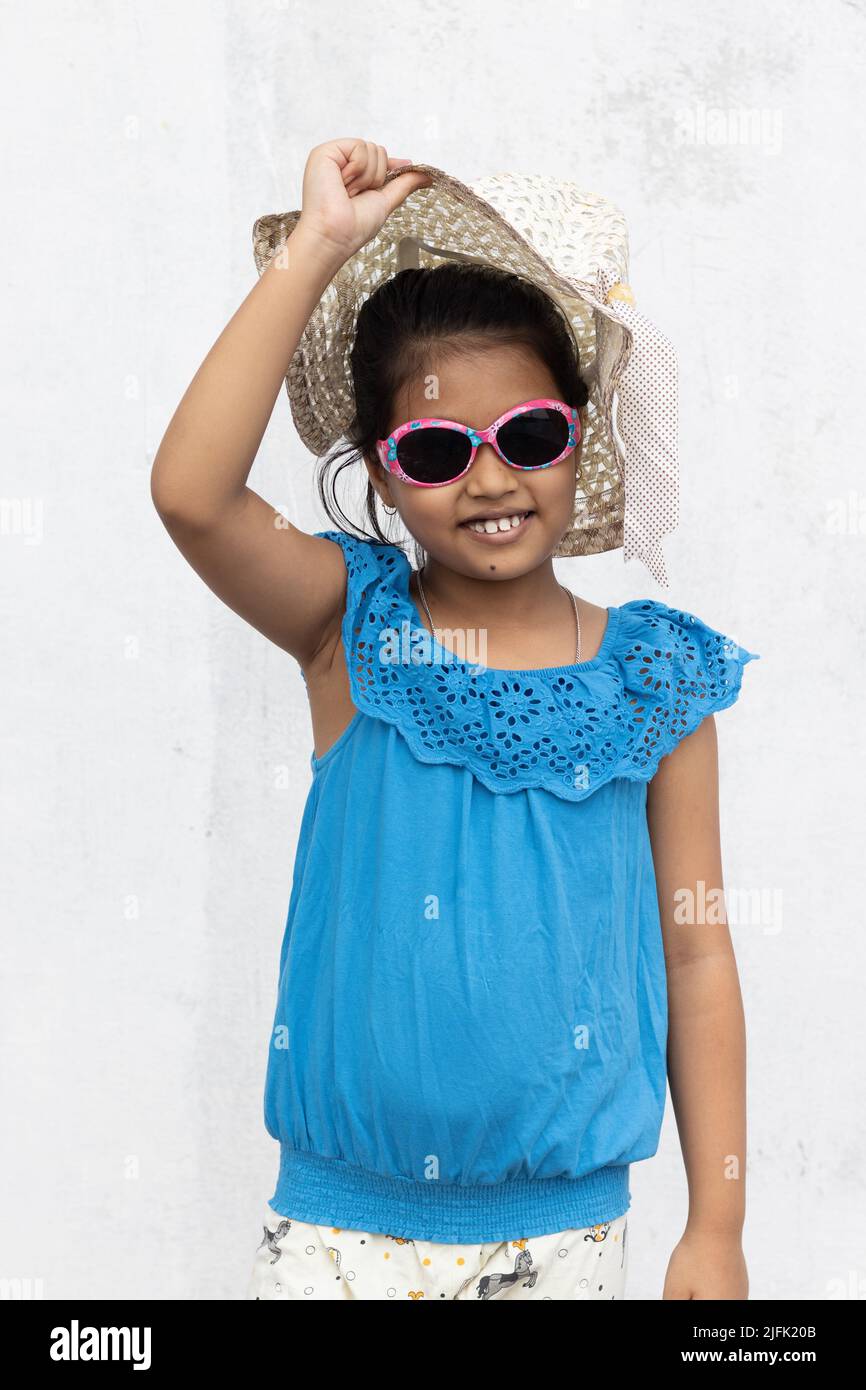 An Indian Girl Wearing Sunglasses And Holding Hat Looking At Camera