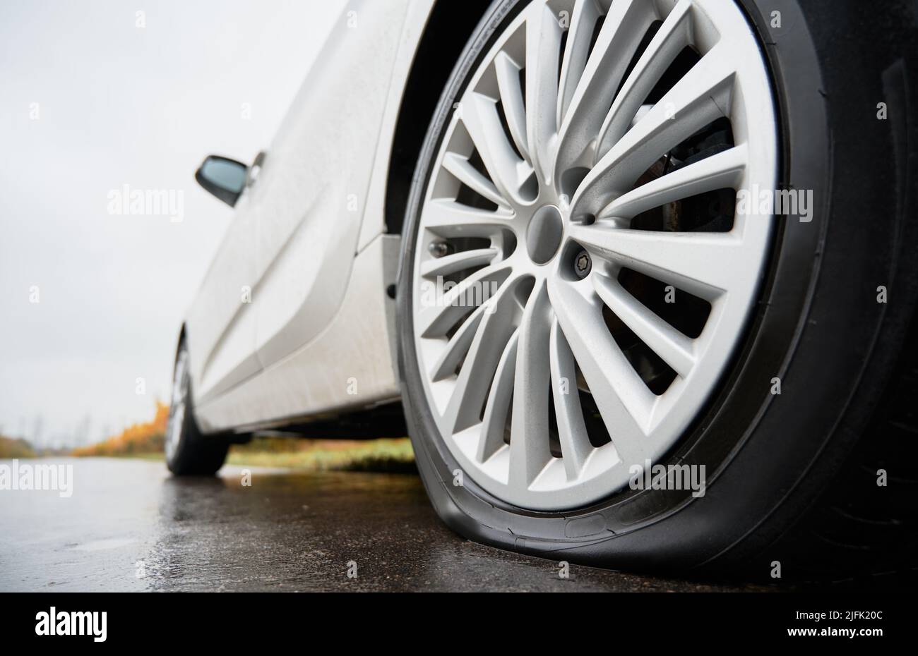 Close up view on stopped white car with punctured car tire on a road ...