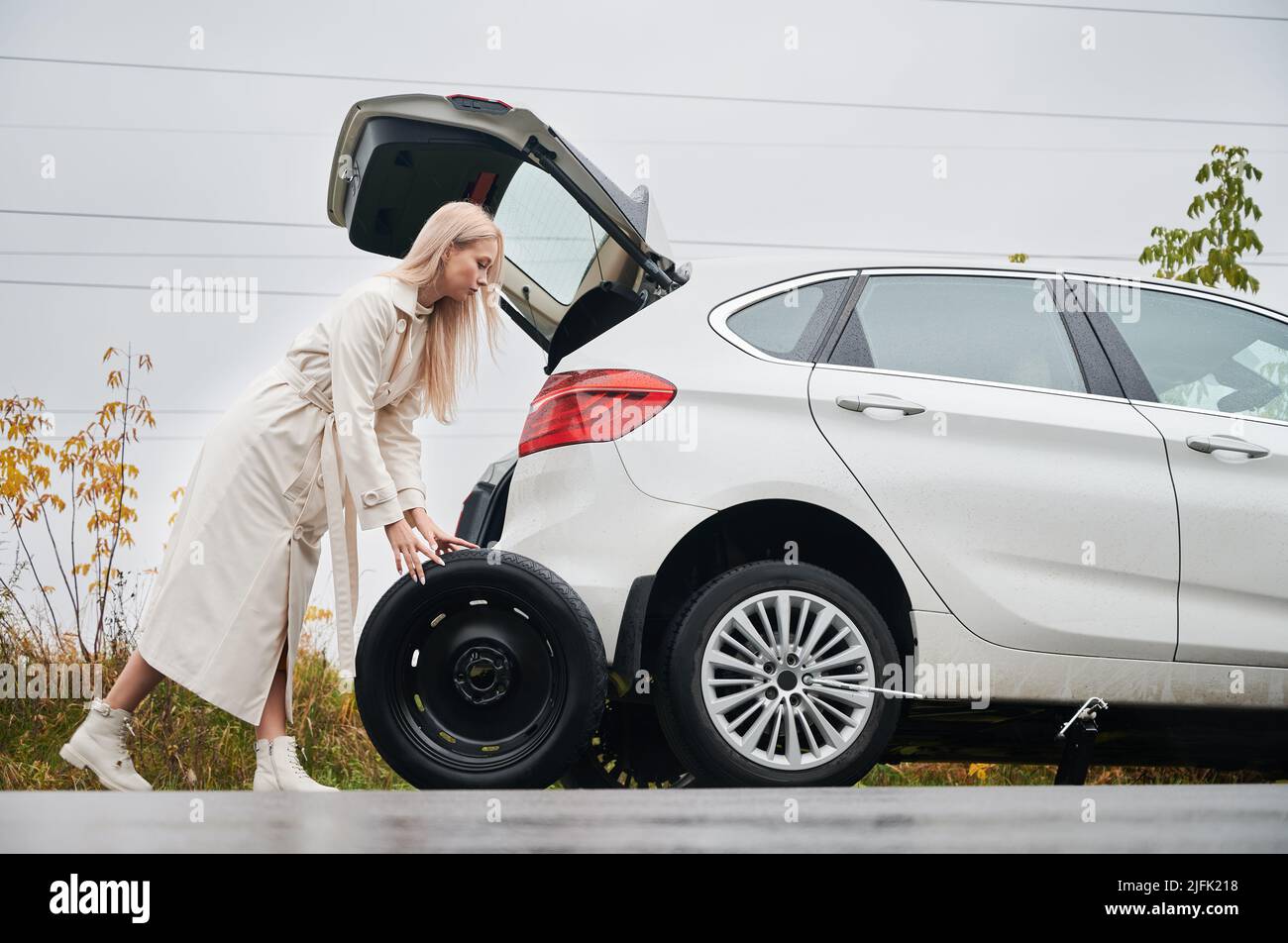 Beautiful woman repairing her white car with punctured car tire, trying ...