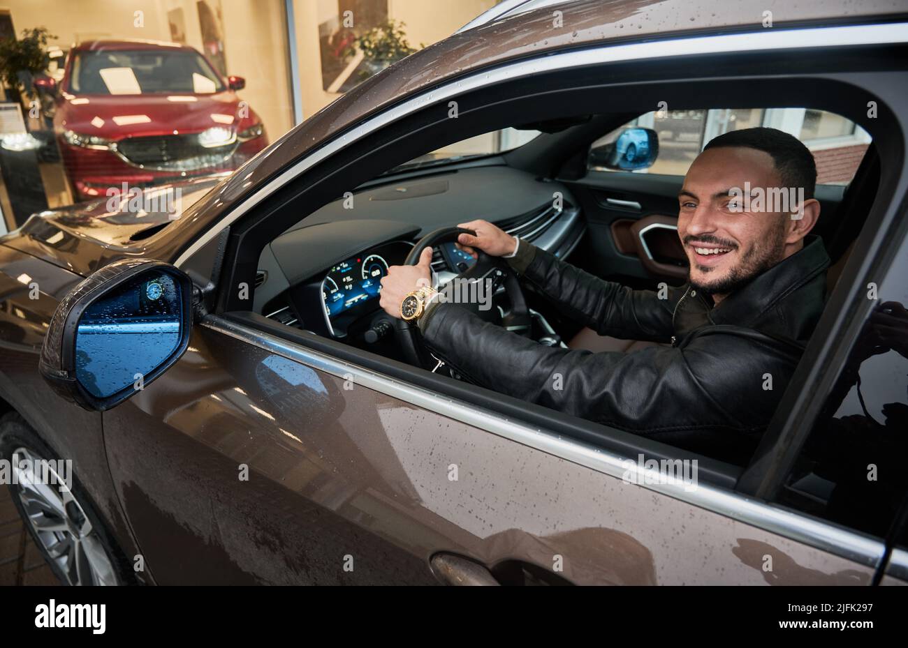 Portrait of handsome young man choosing new car at dealership. Smiling ...