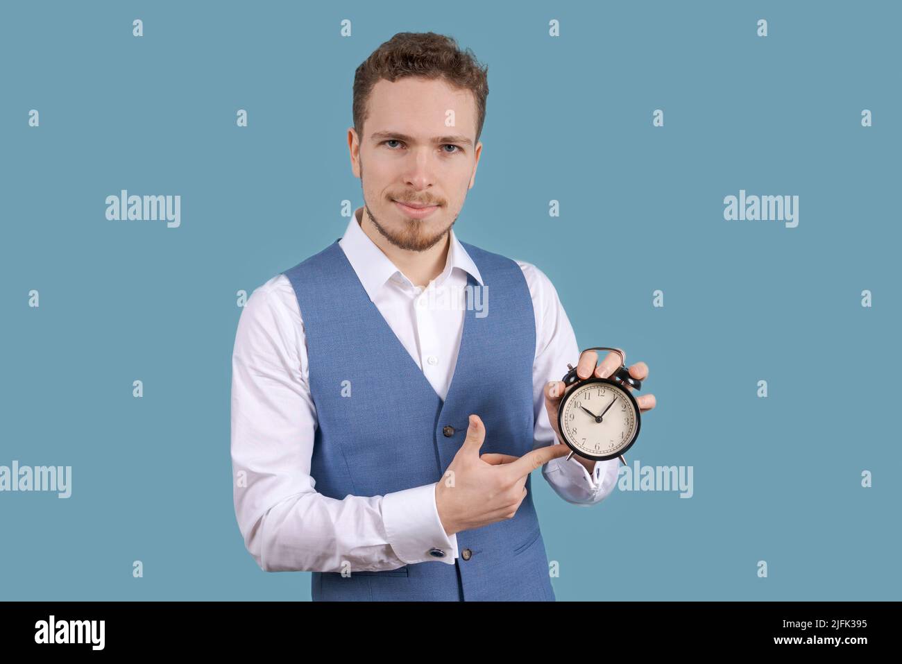 Business man in shirt and blue vest holding an alarm clock on blue ...