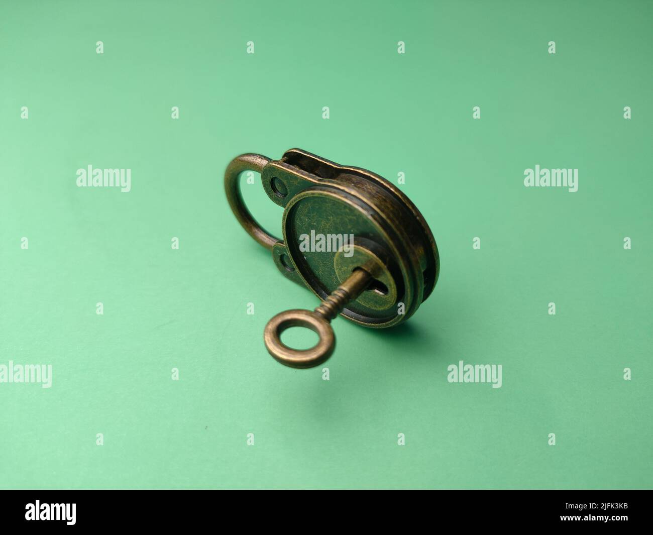 A bronze vintage padlock and a key on soft green paper background with ...